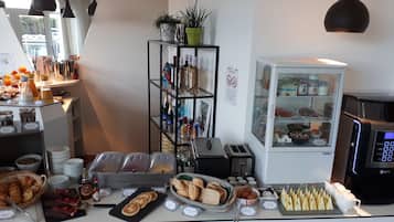 Um buffet de café da manhã com diversos alimentos, uma geladeira e uma máquina de café.