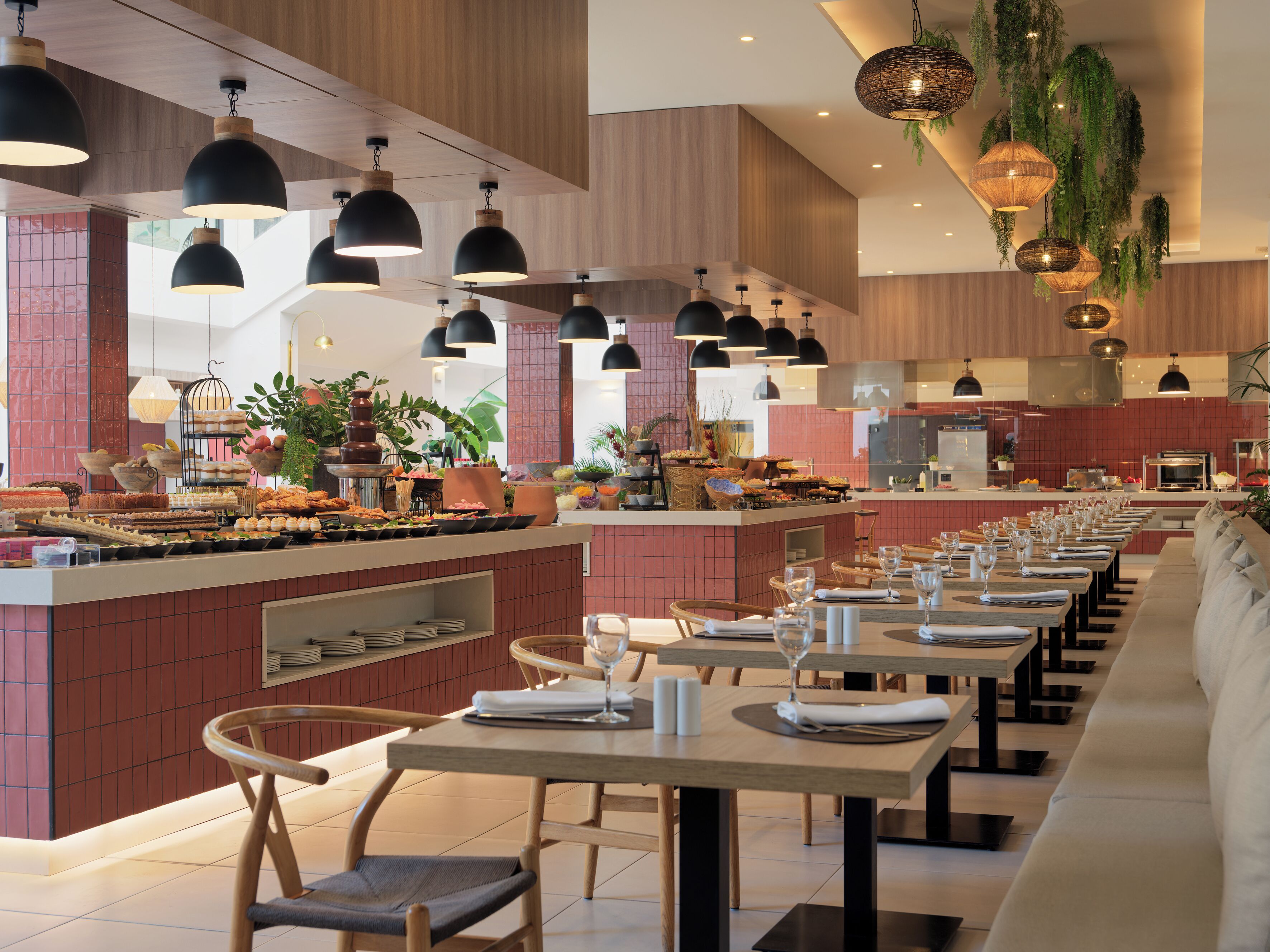 Um restaurante moderno com um balcão comprido, várias mesas de jantar e luminárias pendentes.