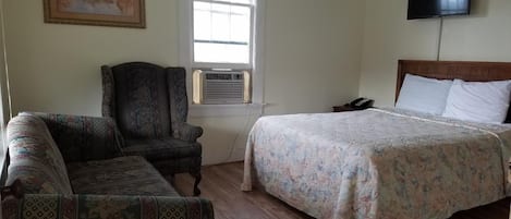 Quarto de hotel com cama, sofá, cadeira, quadro, televisão e ar condicionado.