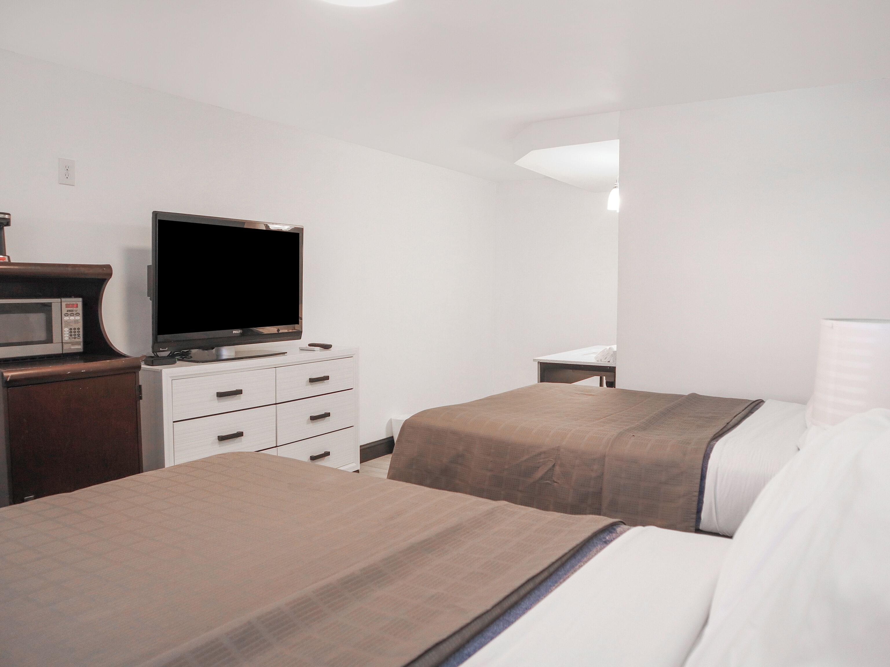 Quarto de hotel com duas camas, televisão, micro-ondas e uma pequena mesa.