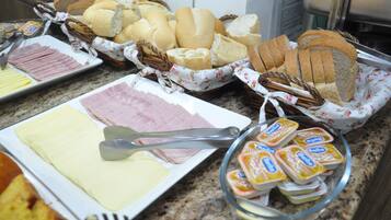 Buffet com diversos alimentos, incluindo pão, queijo e presunto.