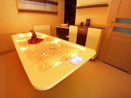 Um spa moderno com uma banheira de pedra aquecida, uma pia pequena e um armário de madeira.