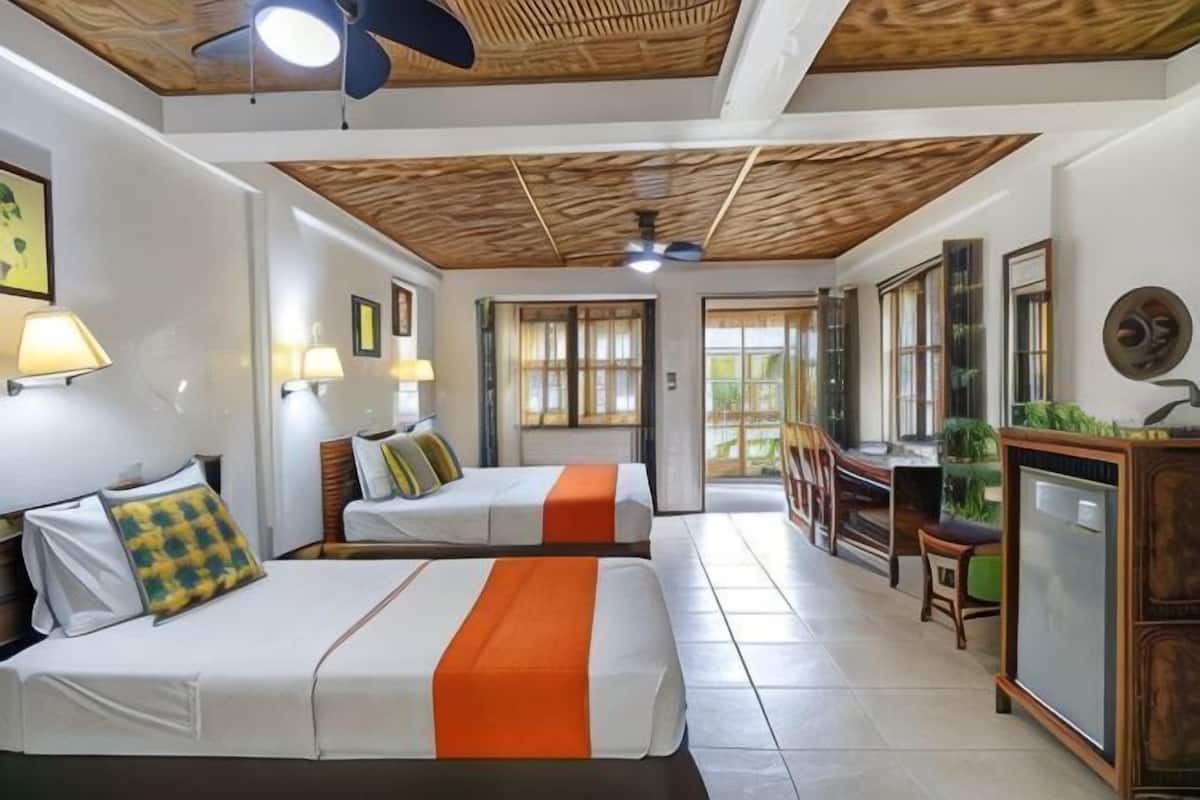 Quarto de hotel com duas camas, uma mesa, uma cadeira e uma televisão.