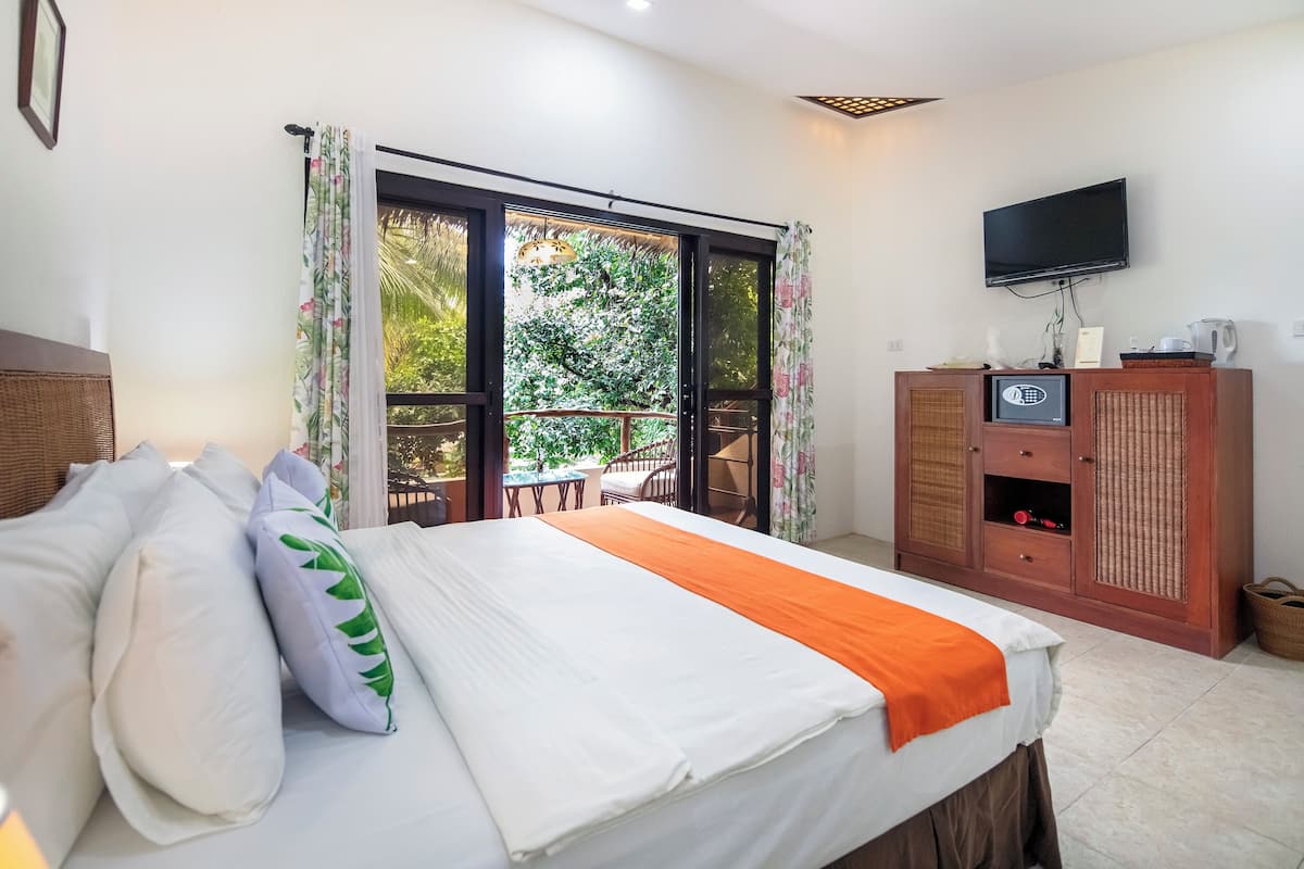 Quarto de hotel com cama, televisão, armário de madeira e varanda com vista para o verde.