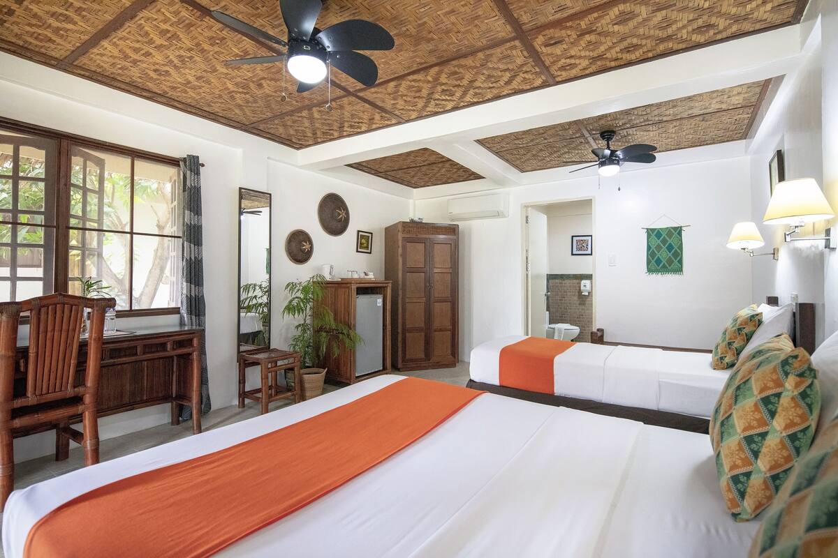 Quarto de hotel com uma cama grande, uma escrivaninha, uma cadeira, um guarda-roupa e um ventilador de teto.