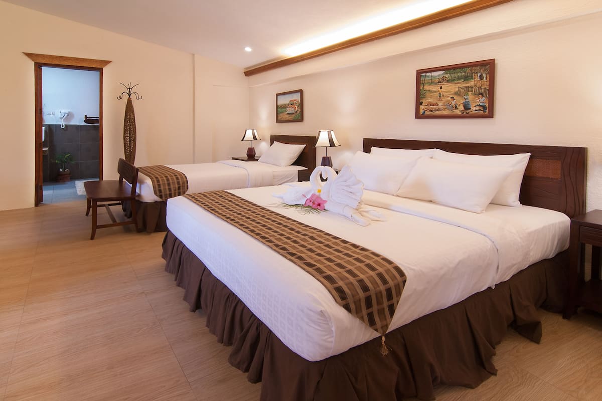 Quarto de hotel com duas camas, piso de madeira, um quadro na parede e porta para o banheiro.