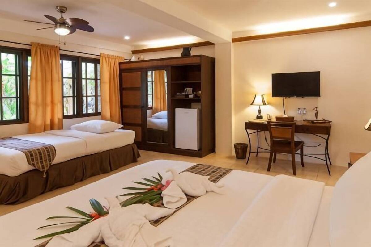 Quarto de hotel com duas camas, uma escrivaninha, uma cadeira, uma televisão e um guarda-roupa.