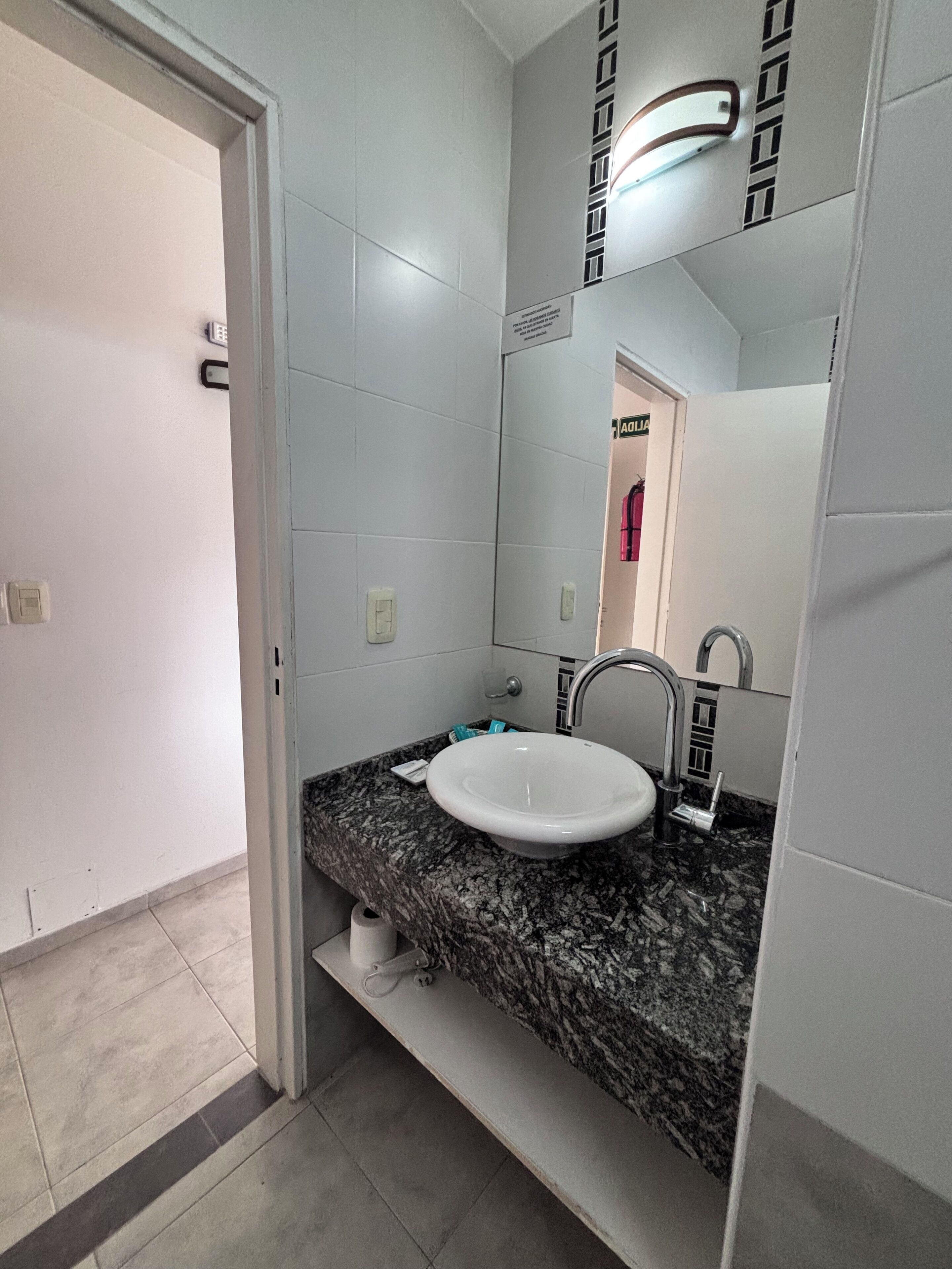 Casa de banho com lavatório branco, bancada de granito e espelho com iluminação.