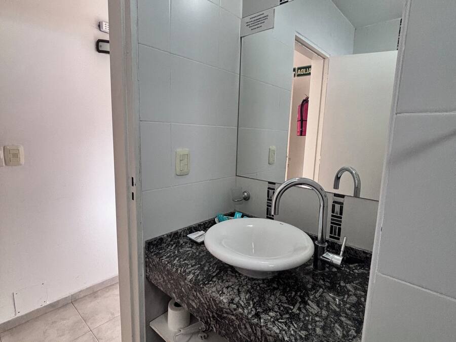 Casa de banho com lavatório branco, bancada de granito e espelho com iluminação.