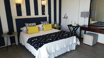 Quarto de hotel com cama, mesas de cabeceira, escrivaninha, cadeira, espelho e um banquinho.
