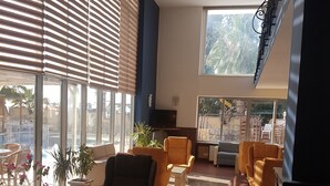Um hall amplo com grandes janelas, assentos confortáveis e uma TV de tela plana.