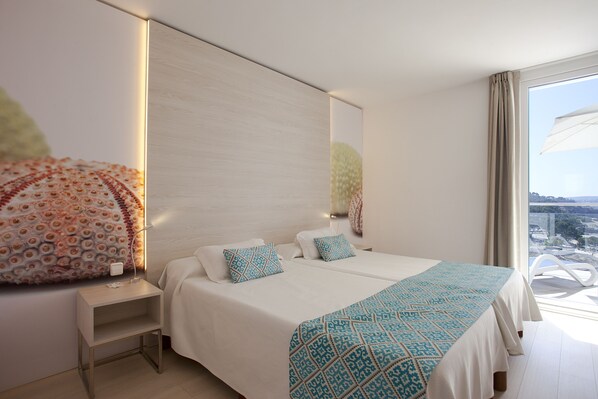Quarto de hotel moderno com cama grande, mesa de cabeceira e vista da cidade através de uma janela ampla.