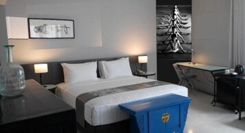 Quarto de hotel com cama, mesas de cabeceira, escrivaninha e uma cadeira.