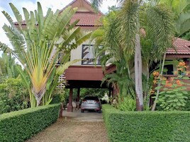 Uma casa com varanda coberta, rodeada por vegetação exuberante e um carro estacionado na frente.