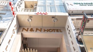Entrada do Hotel N&N com fachada de vidro, escada visível e o número '99' no edifício.