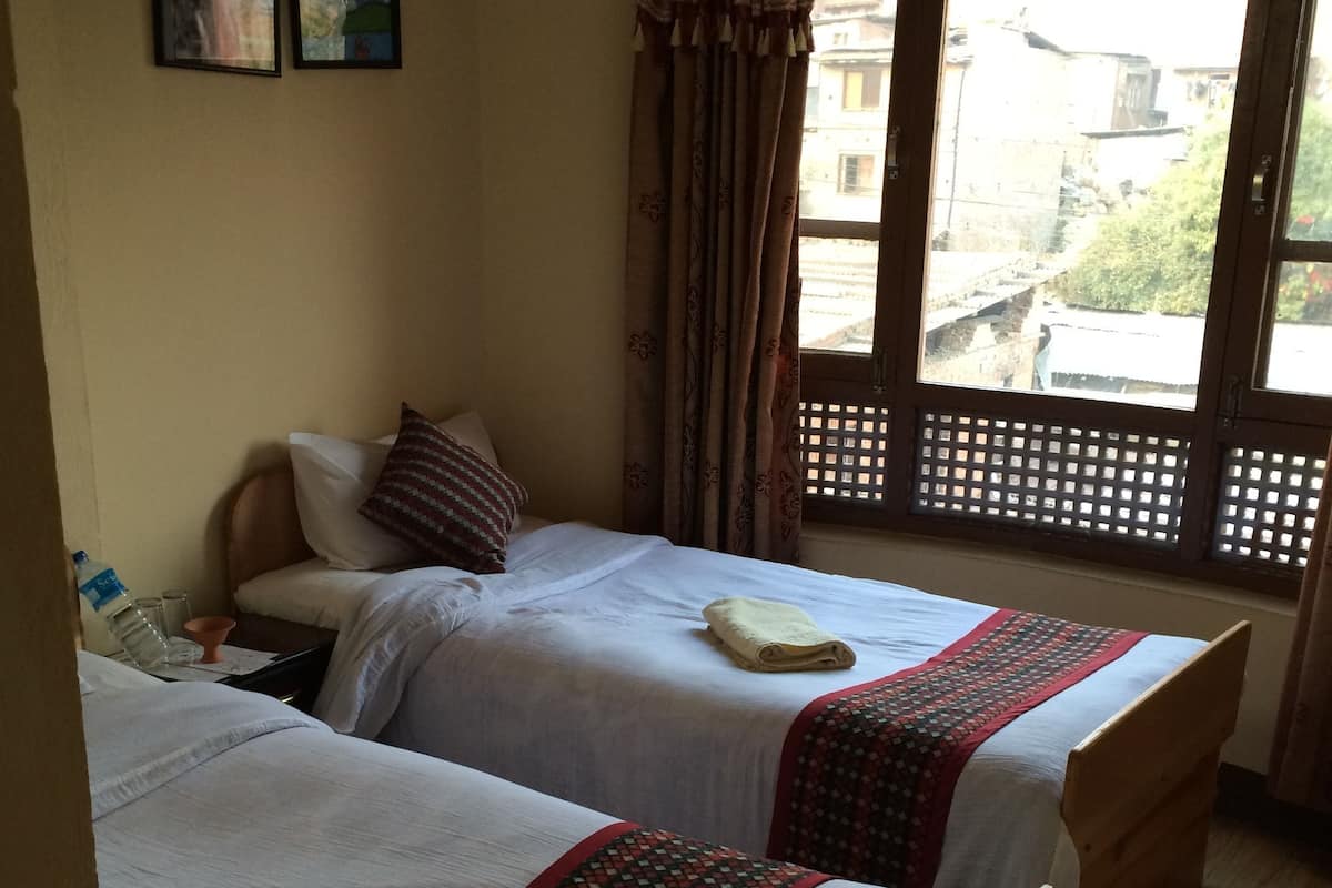 Quarto com duas camas, uma janela com cortinas e vista para prédios.