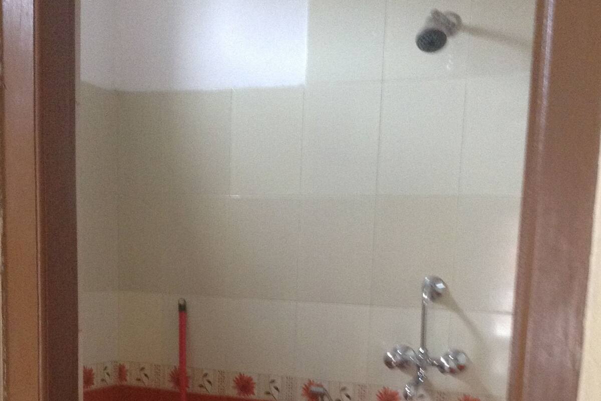 Uma casa de banho pequena com sanita, chuveiro e parede revestida a azulejos vermelhos.