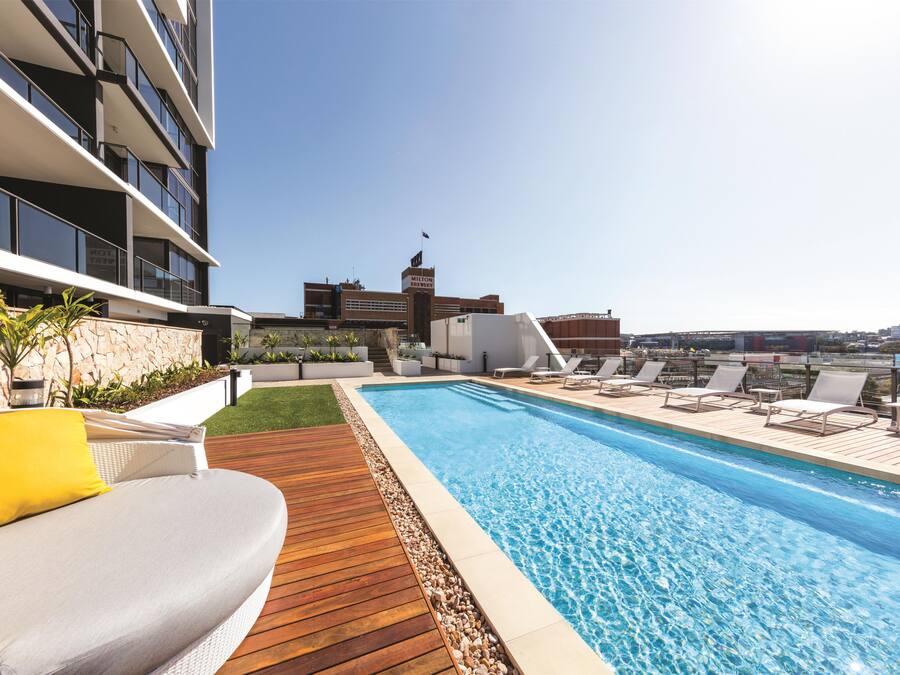 Área de piscina no terraço com cadeiras de descanso e vista para um edifício com a inscrição 'Milton Brewery'.