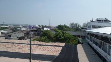 Terraço com cobertura metálica, rodeado por edifícios e árvores.