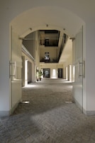 Um corredor amplo com piso de pedra, portas de vidro e escada que leva a um andar superior.