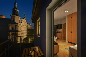 Varanda com vista para um edifício histórico, mesa de madeira com bule e chávena, e interior moderno com armários de madeira e cama.