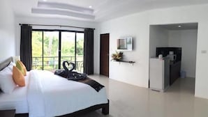 Quarto de hotel moderno com uma cama grande, televisão na parede e cozinha compacta.