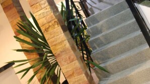 Escadaria com pilares de pedra e corrimão de metal, rodeada por plantas em vasos.