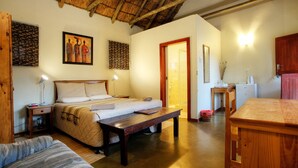 Quarto com cama, um banco de madeira, mesa, sofá e porta que dá para um banheiro.