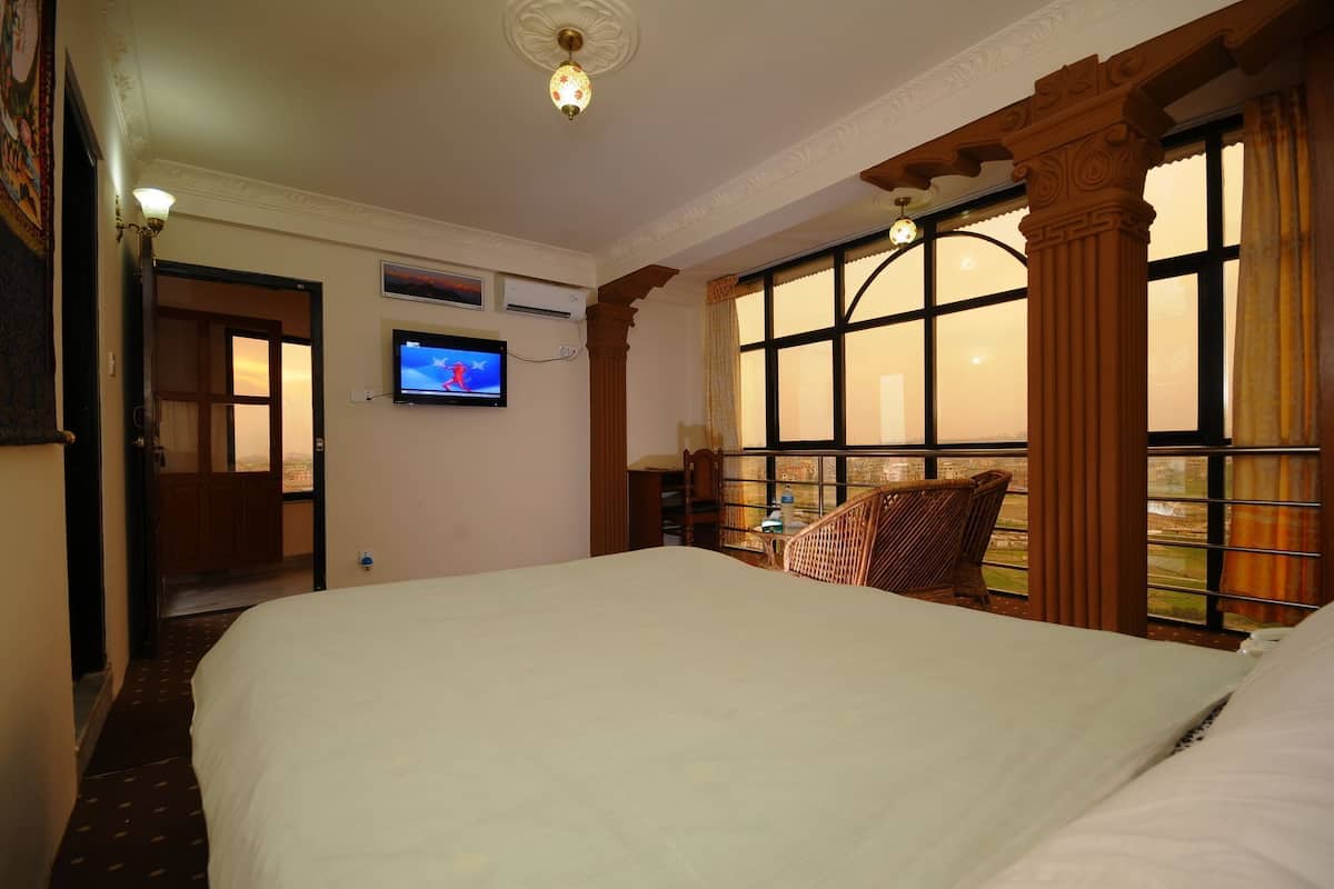 Quarto de hotel com uma cama grande, televisão, janela com cortinas e escadas para um andar superior.