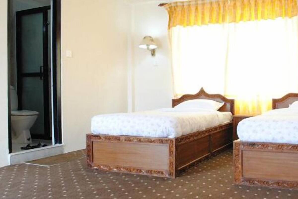Quarto com duas camas de madeira, porta de banheiro e cortina.