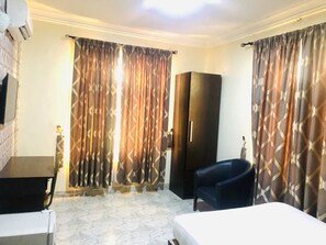 Quarto de hotel com cama, escrivaninha, cadeira, guarda-roupa e cortinas estampadas.