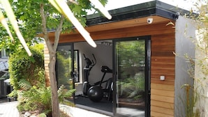 Um edifício moderno com fachada de madeira, grandes portas de vidro e área externa para exercícios com bicicletas ergométricas e uma bola de ginástica grande.