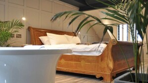 Quarto com cama de madeira, roupa de cama branca e uma planta em vaso.