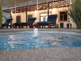Piscina com uma fonte, rodeada por espreguiçadeiras e uma área coberta com luzes de corda.