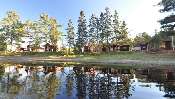 Um terreno à beira do lago com cabanas e reflexo na água.