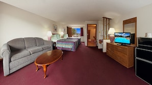 Quarto de hotel com sofá, cama com colcha colorida, televisão e cômoda de madeira.
