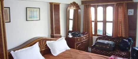 Quarto de hotel com uma cama, cômoda, espelho e janela com cortinas.