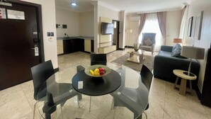 Uma sala de estar moderna com uma mesa de jantar de vidro, cadeiras pretas, um sofá e uma televisão.