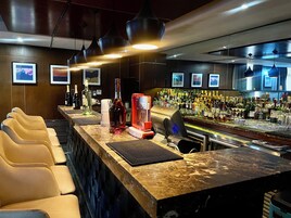 Uma área de bar com bancada de mármore, diversas garrafas de bebidas e um espaço de estar com cadeiras estofadas.