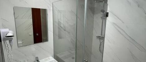 Um banheiro moderno com box de vidro, parede revestida em mármore e pia branca.