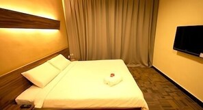 Quarto de hotel com cama bem arrumada, televisão de tela plana na parede e cabeceira de madeira.