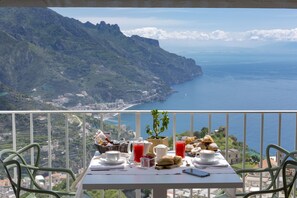 Mesa posta com itens de café da manhã e vista para o mar e montanhas.