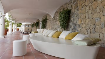 Uma área de estar moderna ao ar livre, com parede de pedra e sofá branco com almofadas.