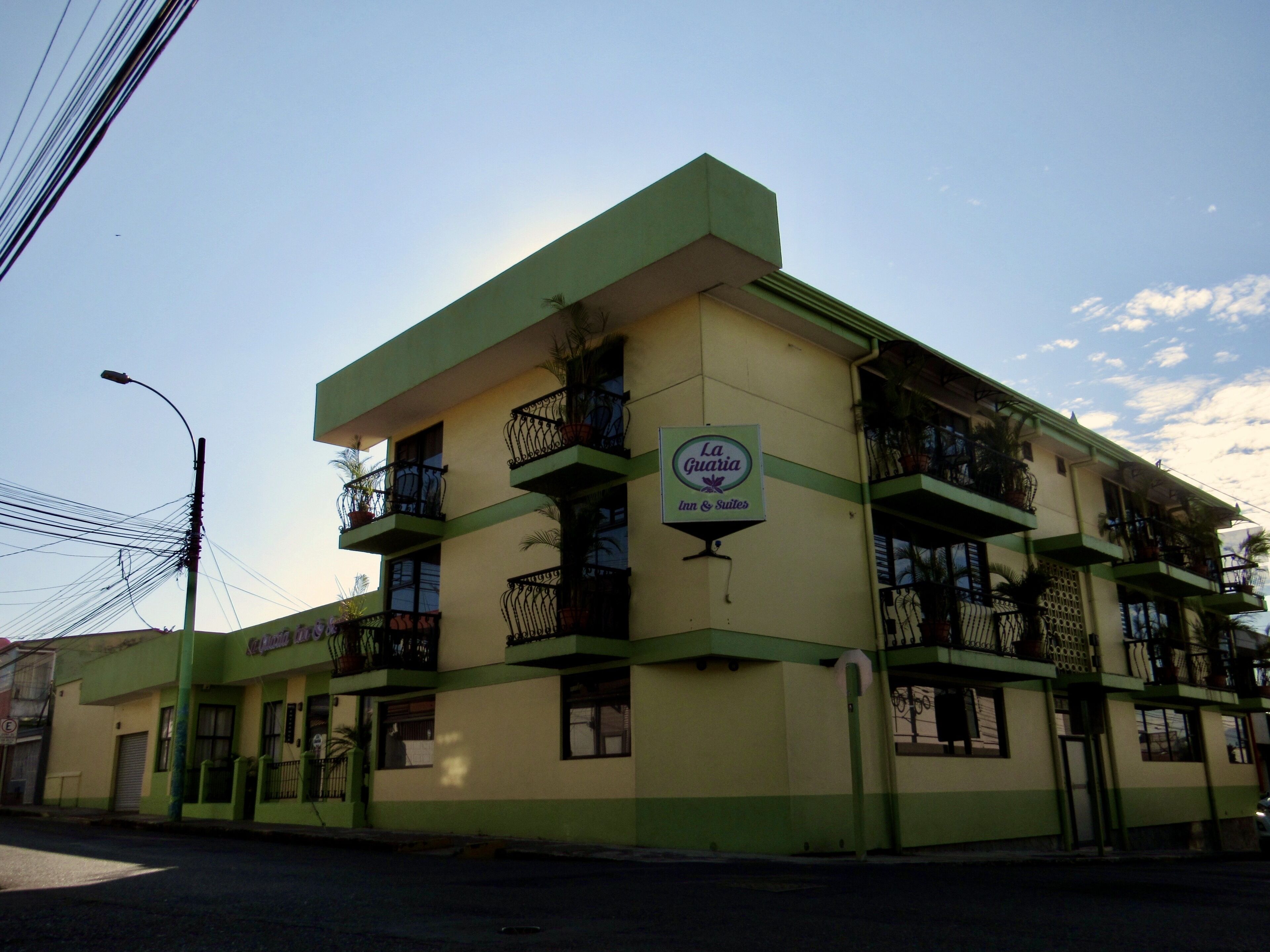 Um edifício de vários andares com varandas, um letreiro com 'La Guaria Inn & Suites' e um poste de luz em primeiro plano.