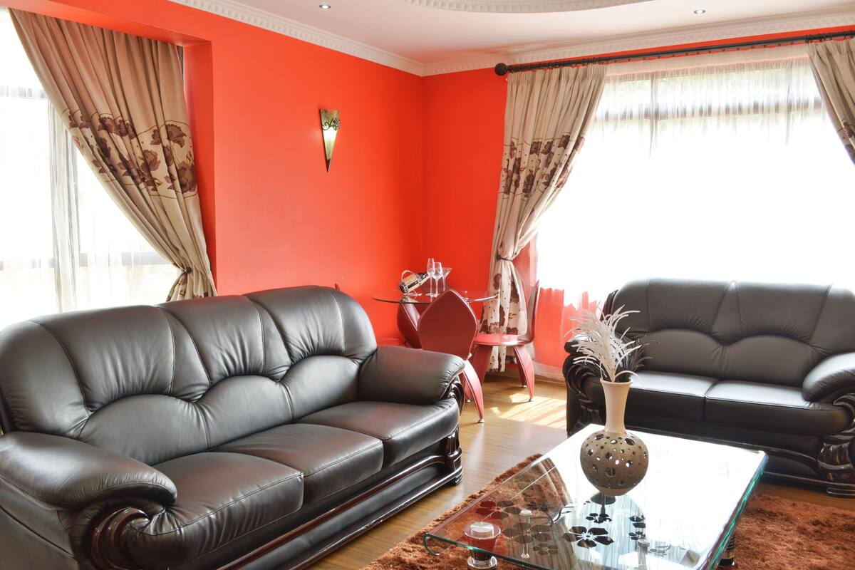 Uma sala de estar com dois sofás de couro preto, uma mesa de centro de vidro e uma parede com destaque em vermelho.
