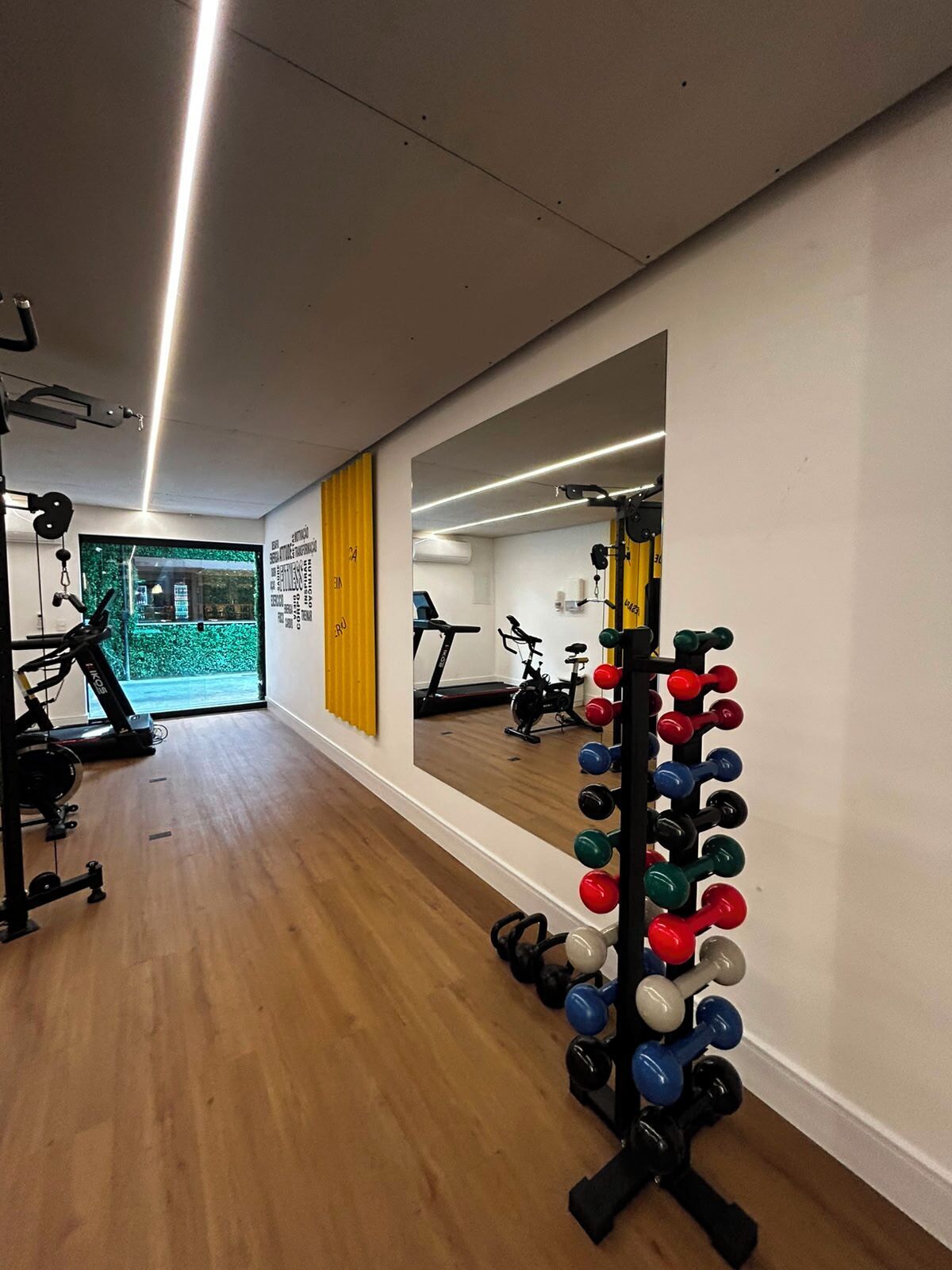 Uma academia com equipamentos de ginástica, espelho e suporte de halteres.