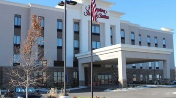 Um hotel moderno com telhado plano, várias janelas e a placa da Hampton Inn Suites.