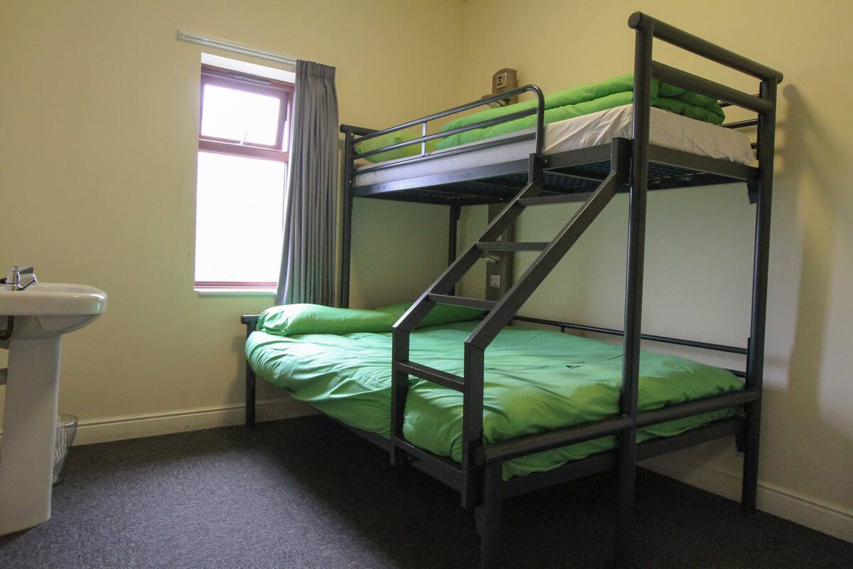 Uma cama beliche com roupa de cama verde em um quarto com janela e pia.