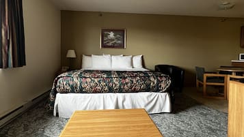 Quarto de hotel com cama, escrivaninha, cadeira, mesa e um quadro na parede.