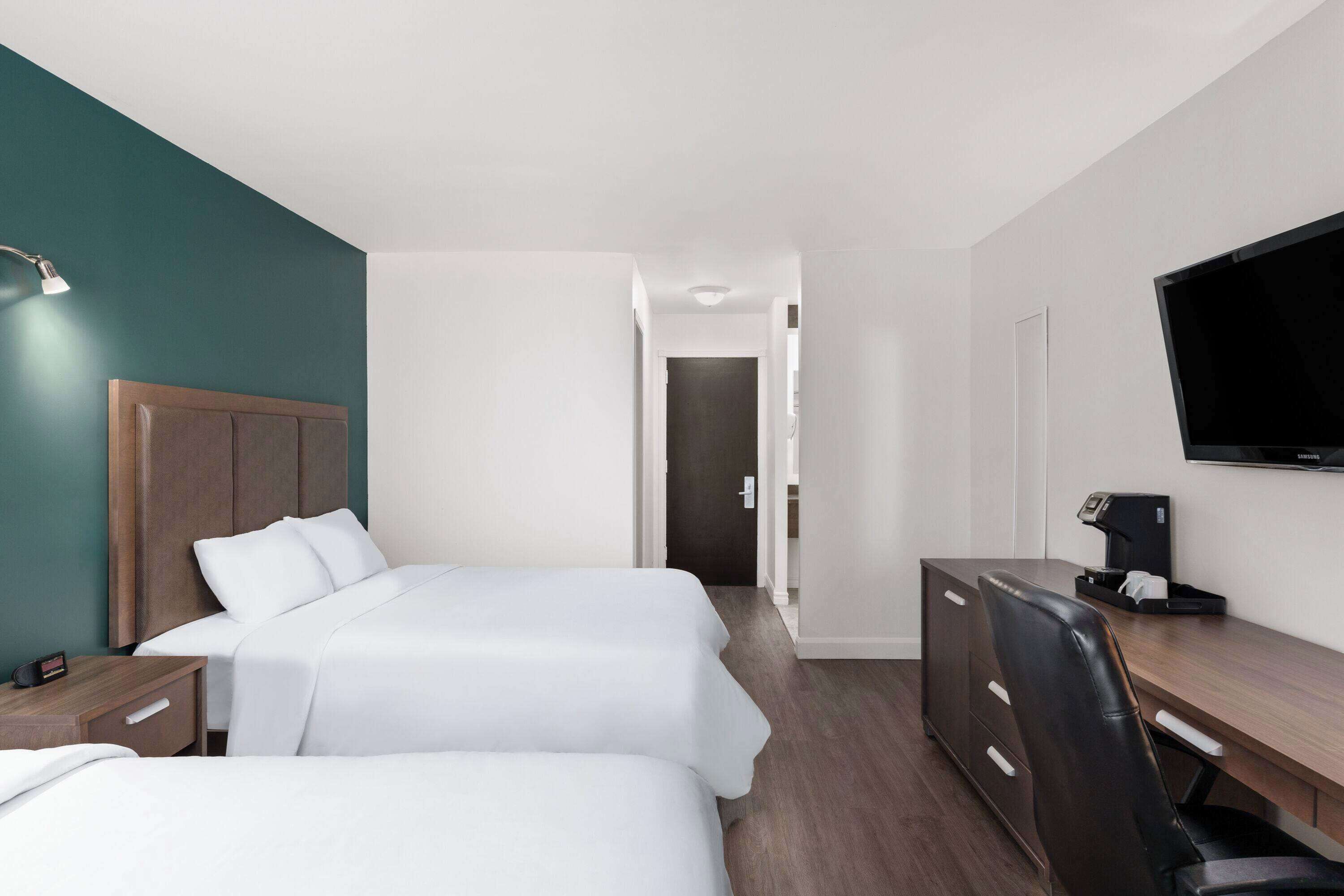 Quarto de hotel com duas camas, uma escrivaninha, uma cadeira, uma televisão e uma máquina de café.